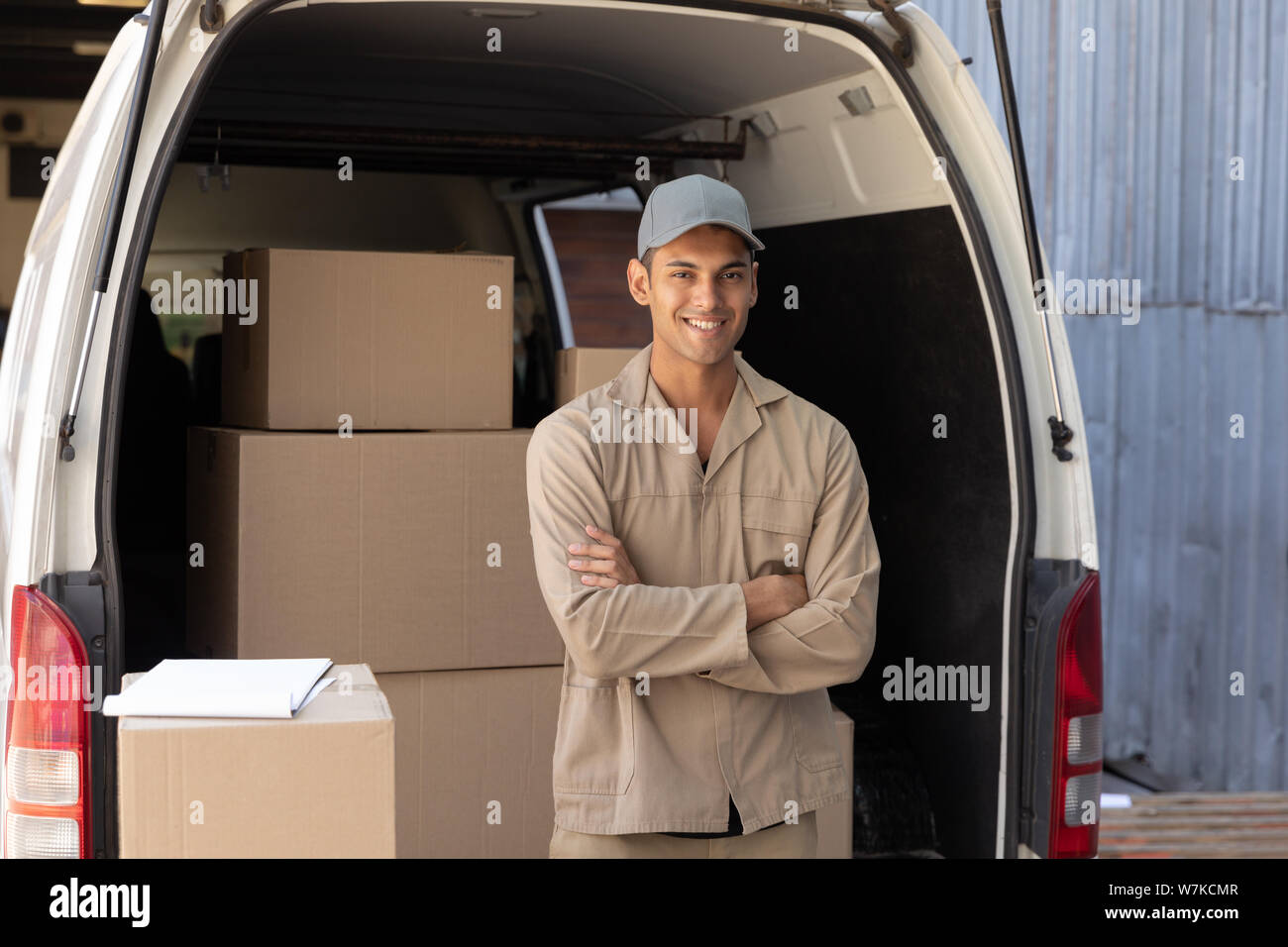 Delivery man standing with arms crossed near van outside the warehouse ...