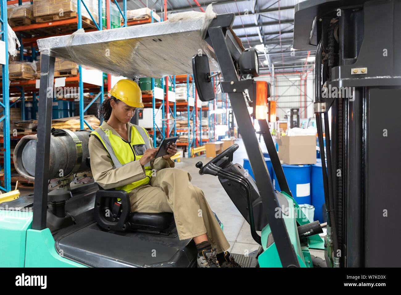 Female staff using digital tablet while sitting on forklift Stock Photo ...