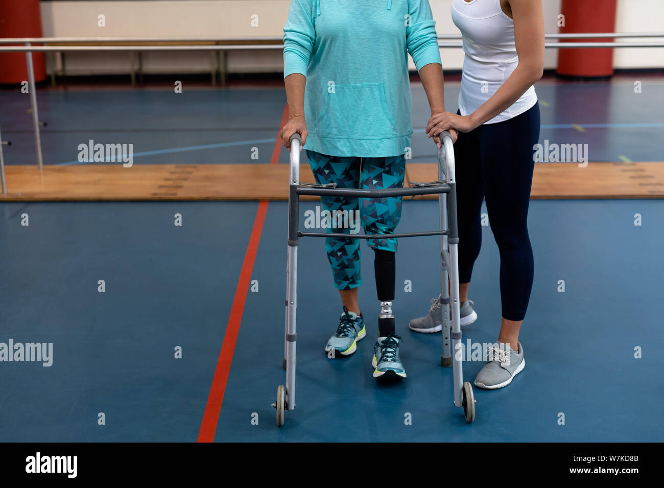 Female physiotherapist helping disabled senior woman walk with walker ...