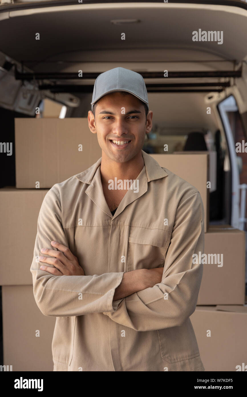 Delivery man standing with arms crossed near van outside the warehouse ...