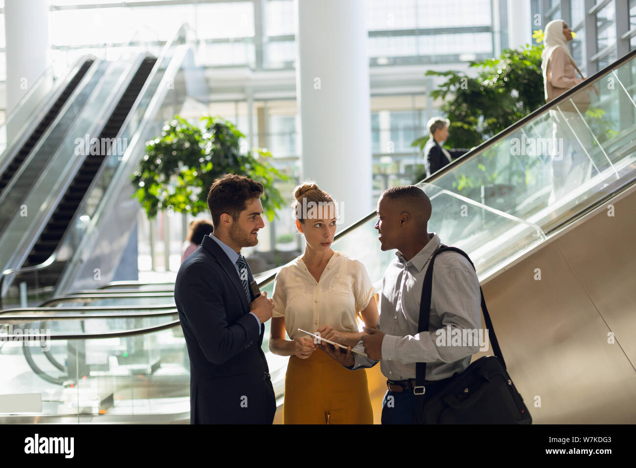 Diverse young business people with tablet talking in a modern atrium ...