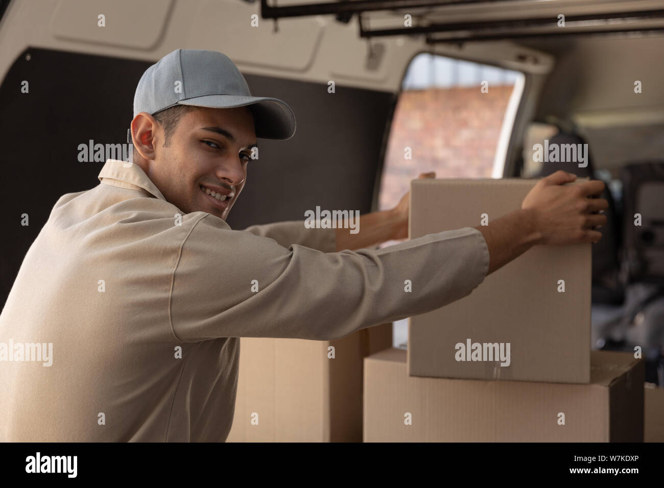 Delivery man unloading cardboard boxes from a van outside the warehouse ...