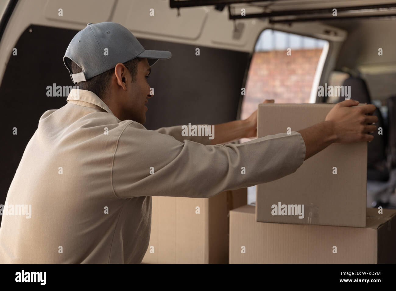 Delivery man unloading cardboard boxes from a van outside the warehouse ...