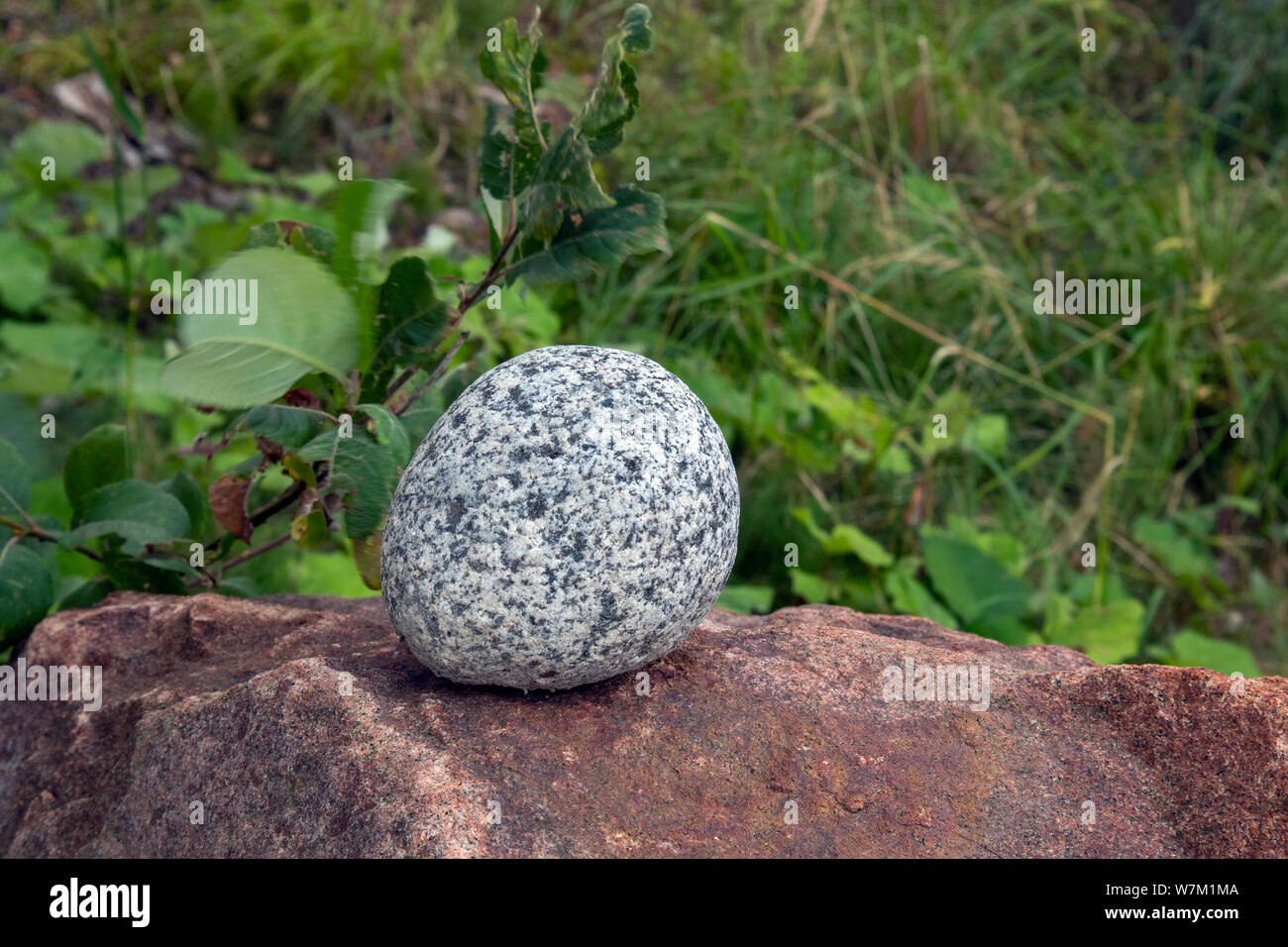 Round gray stone on top of brown boulder outdoors Stock Photo - Alamy