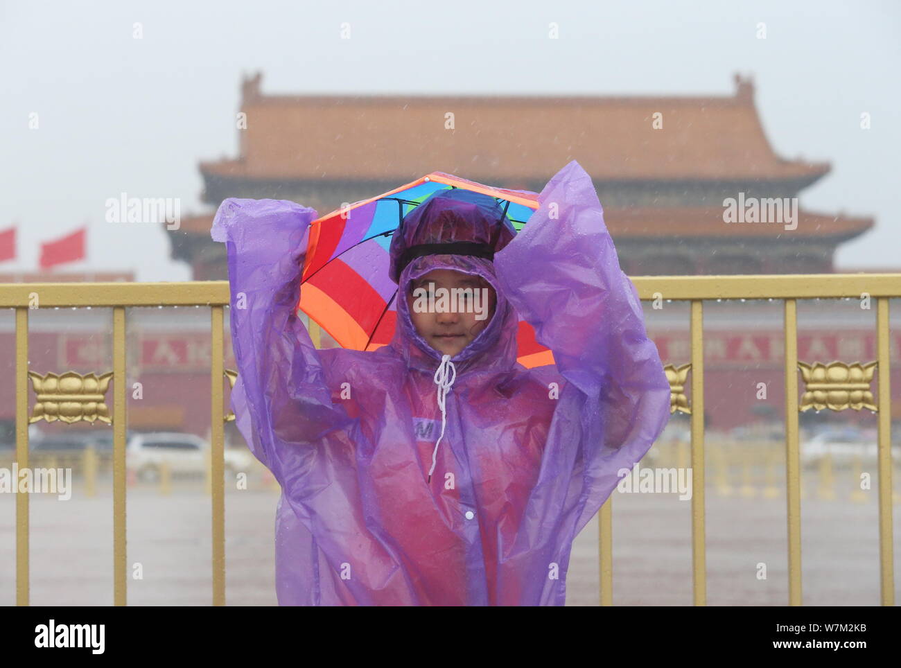 A tourist wearing an umbrella hat and a rain coat poses for a photo in ...