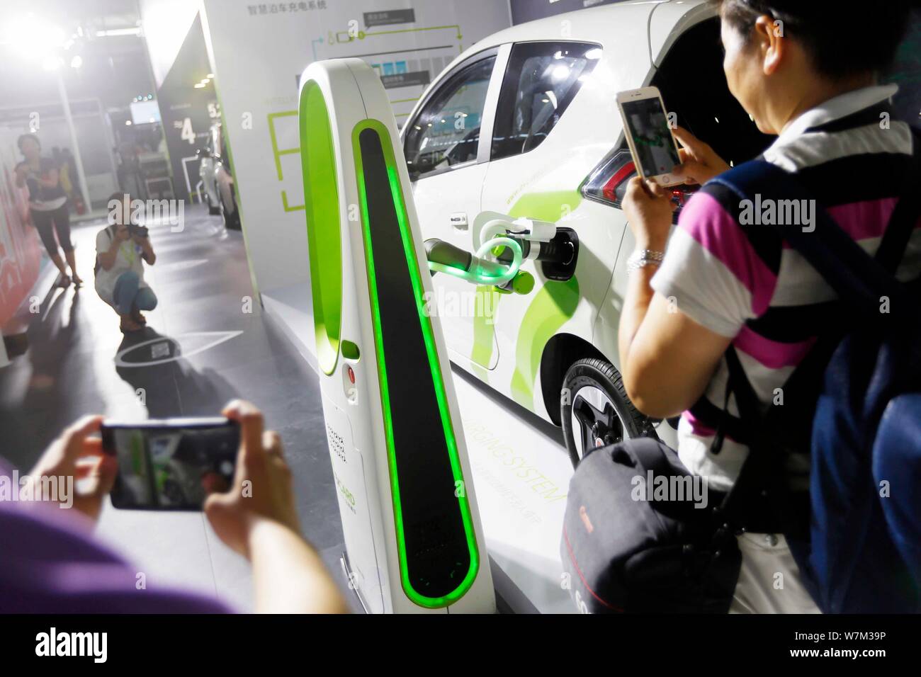 Visitors take photos of an EV of EVCard electric car sharing service being charged by automatic ...