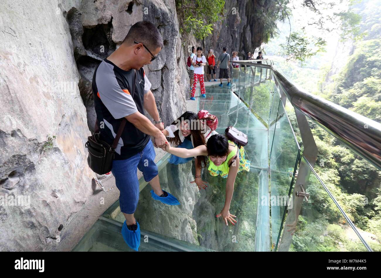 Tourists climb on a glass-made plank road built along a cliff at Shimen ...