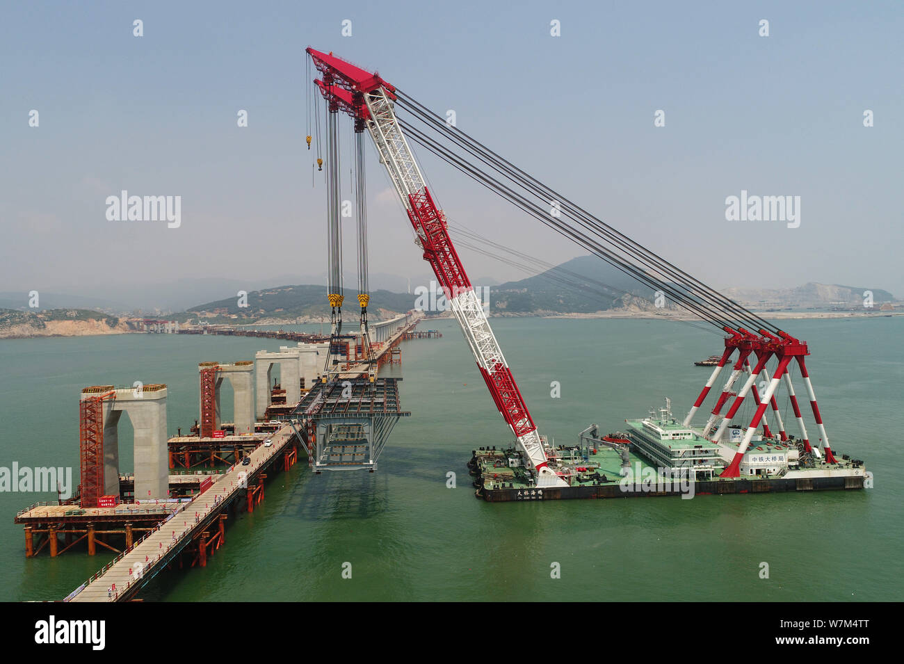 A crane ship lifts the first steel truss girder to the bridge piers of ...