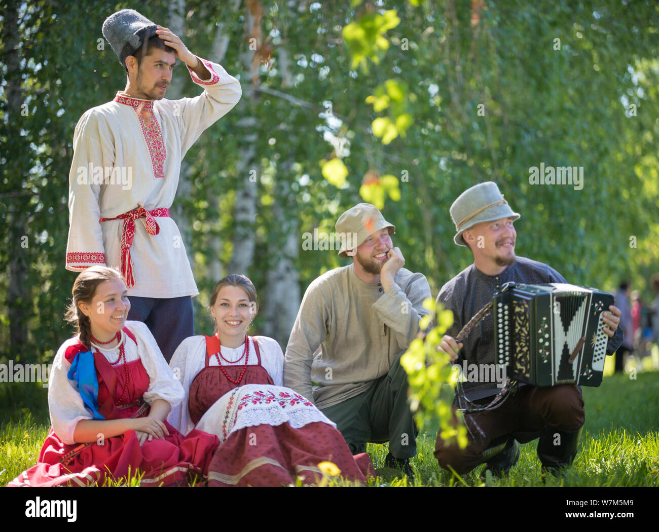 People in traditional Russian clothes sit on the lawn - one of them ...