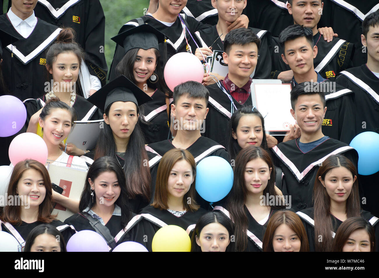 Graduates dressed in academic gowns holding ballons pose for a group ...