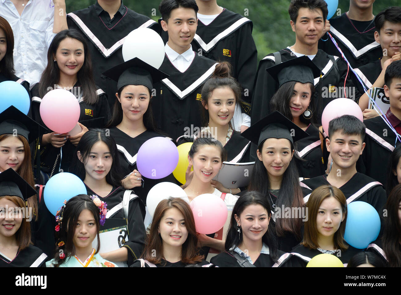 Graduates dressed in academic gowns holding ballons pose for a group ...