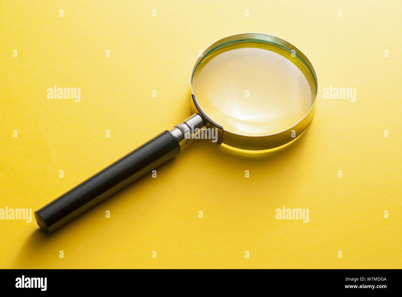 Magnifying glass lying diagonally on yellow with copy space viewed from ...