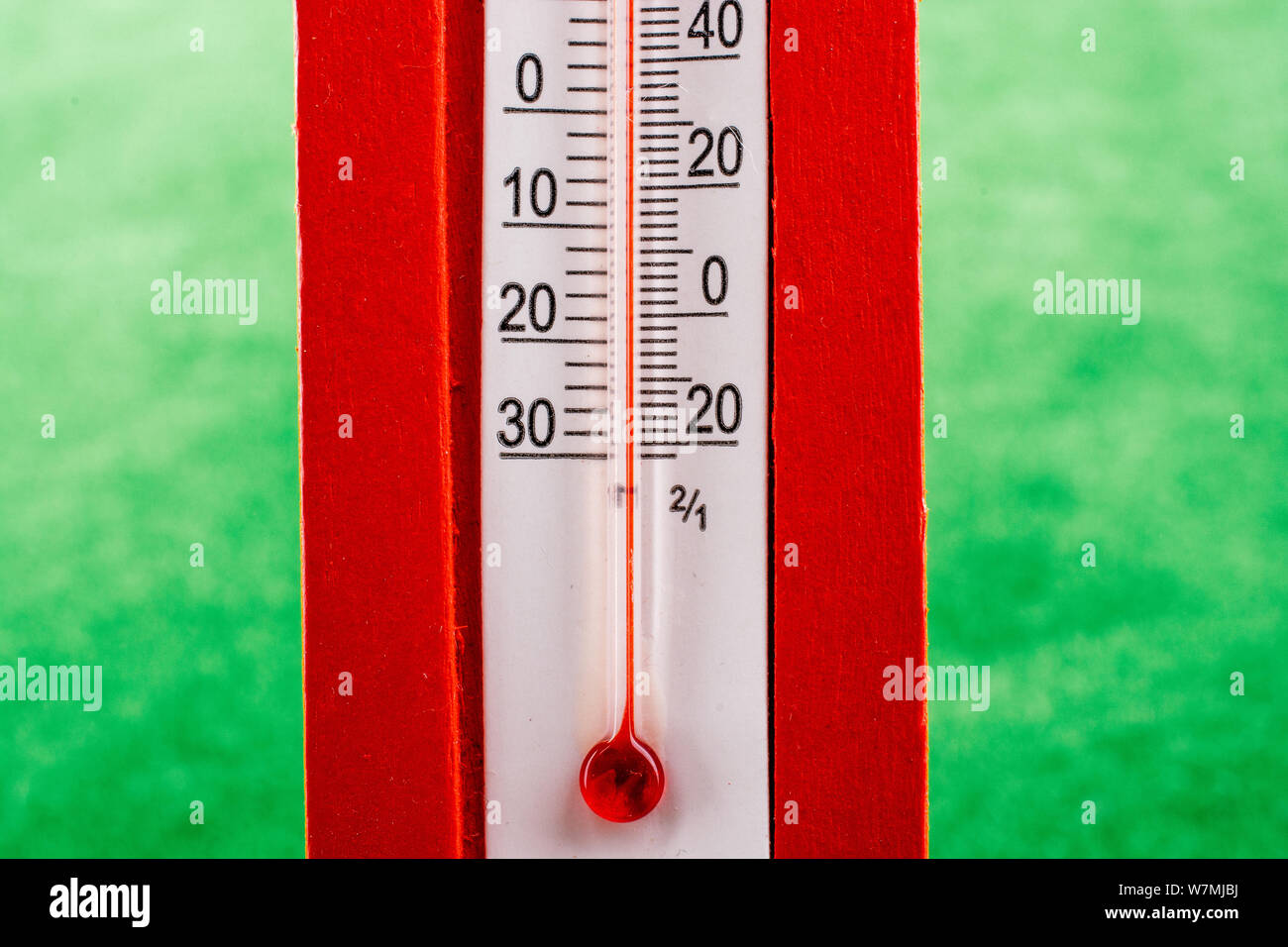 A red plastic thermometer on a green background Stock Photo - Alamy