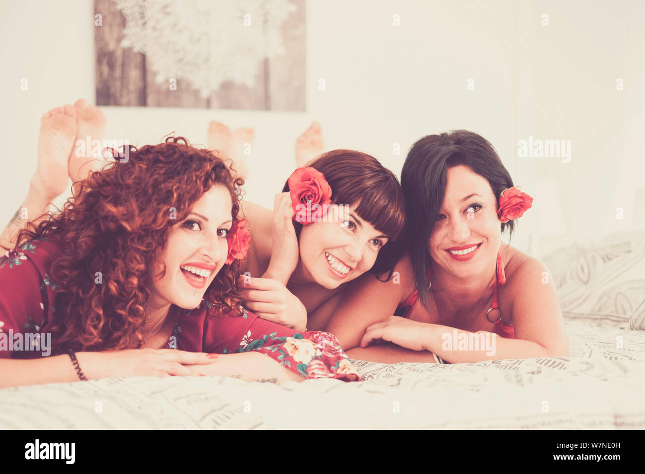 Group of three young cheerful women have fun together laying on the bed ...