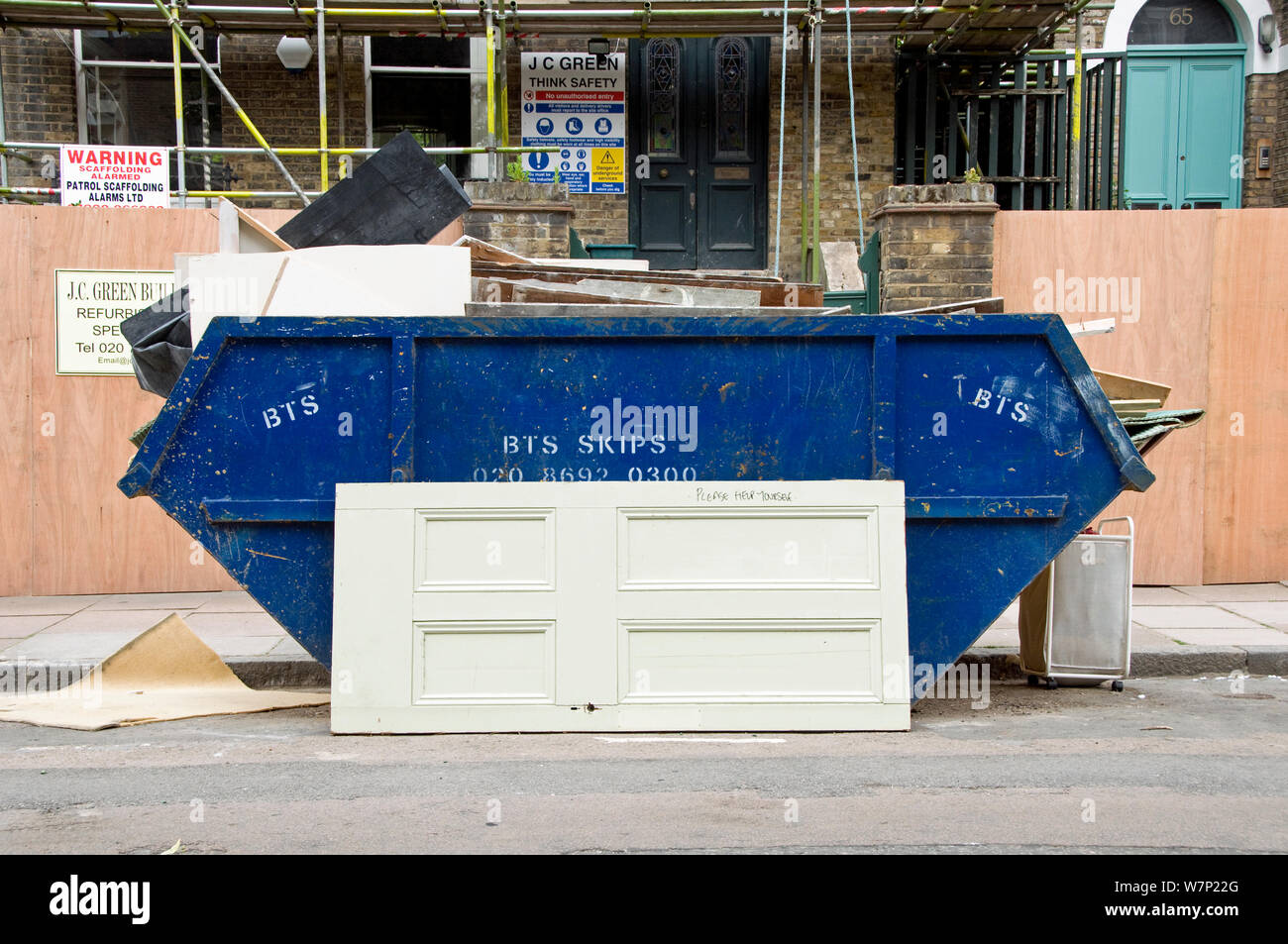 Old door in front of skip offered for recycling with a note saying ...