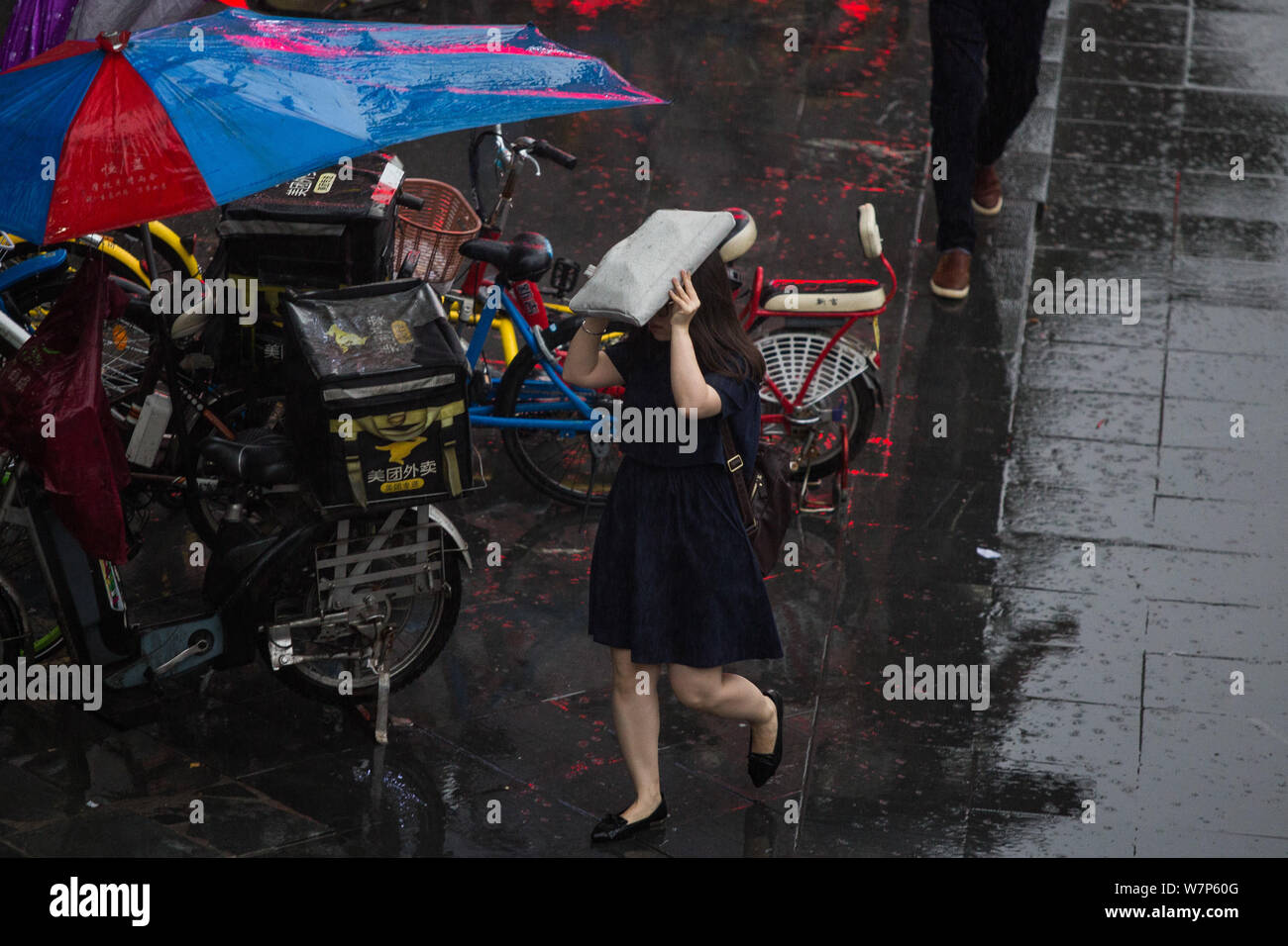 A Chinese commuter shields herself with her bag from heavy rain caused ...