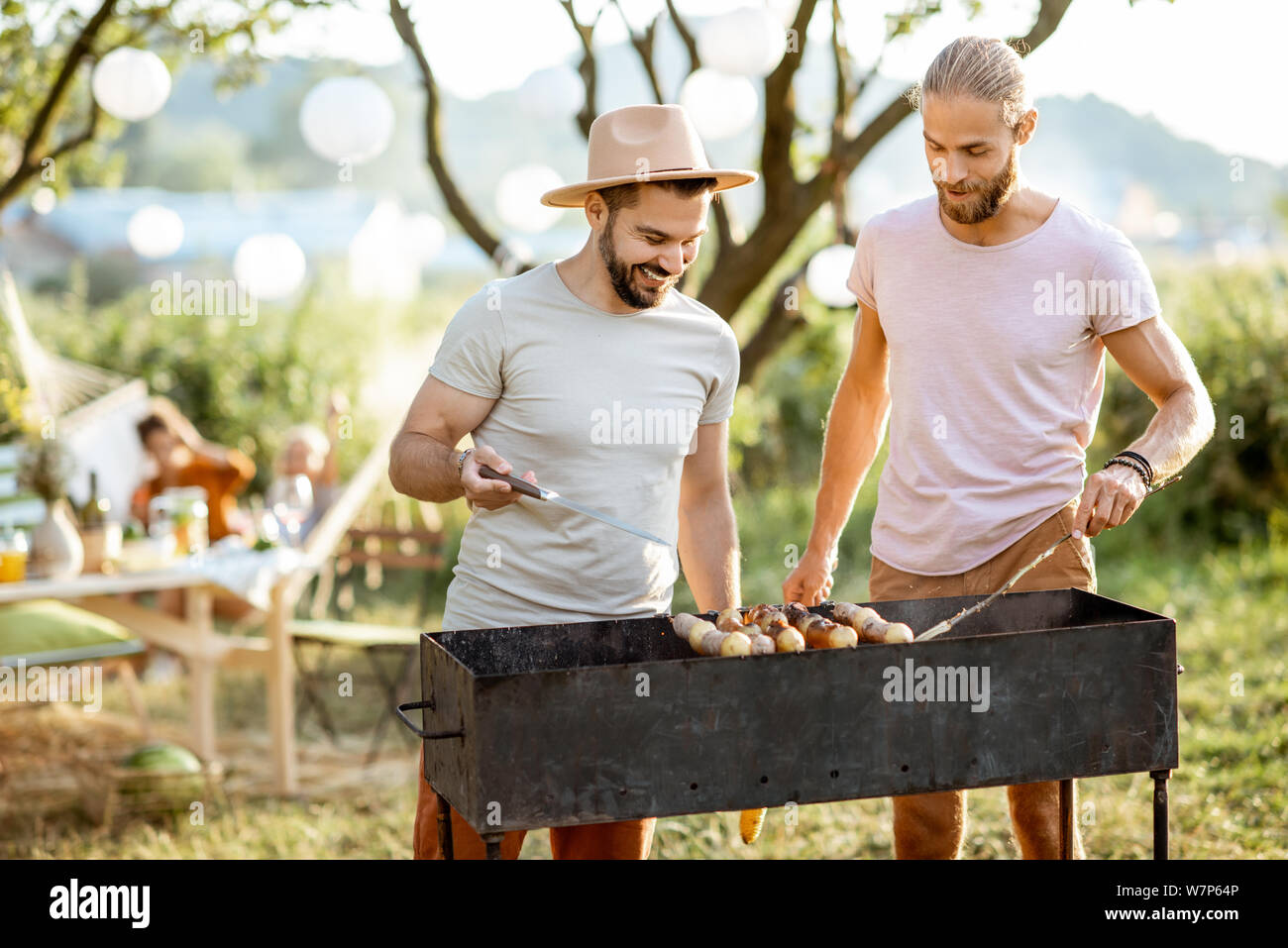 Two male friends cooking food on a barbecue in the beautiful garden ...