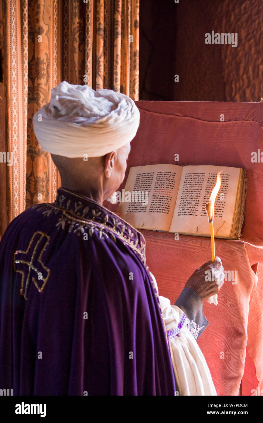 Priest holding a candle and reading the 900 year old Holy Book of ...