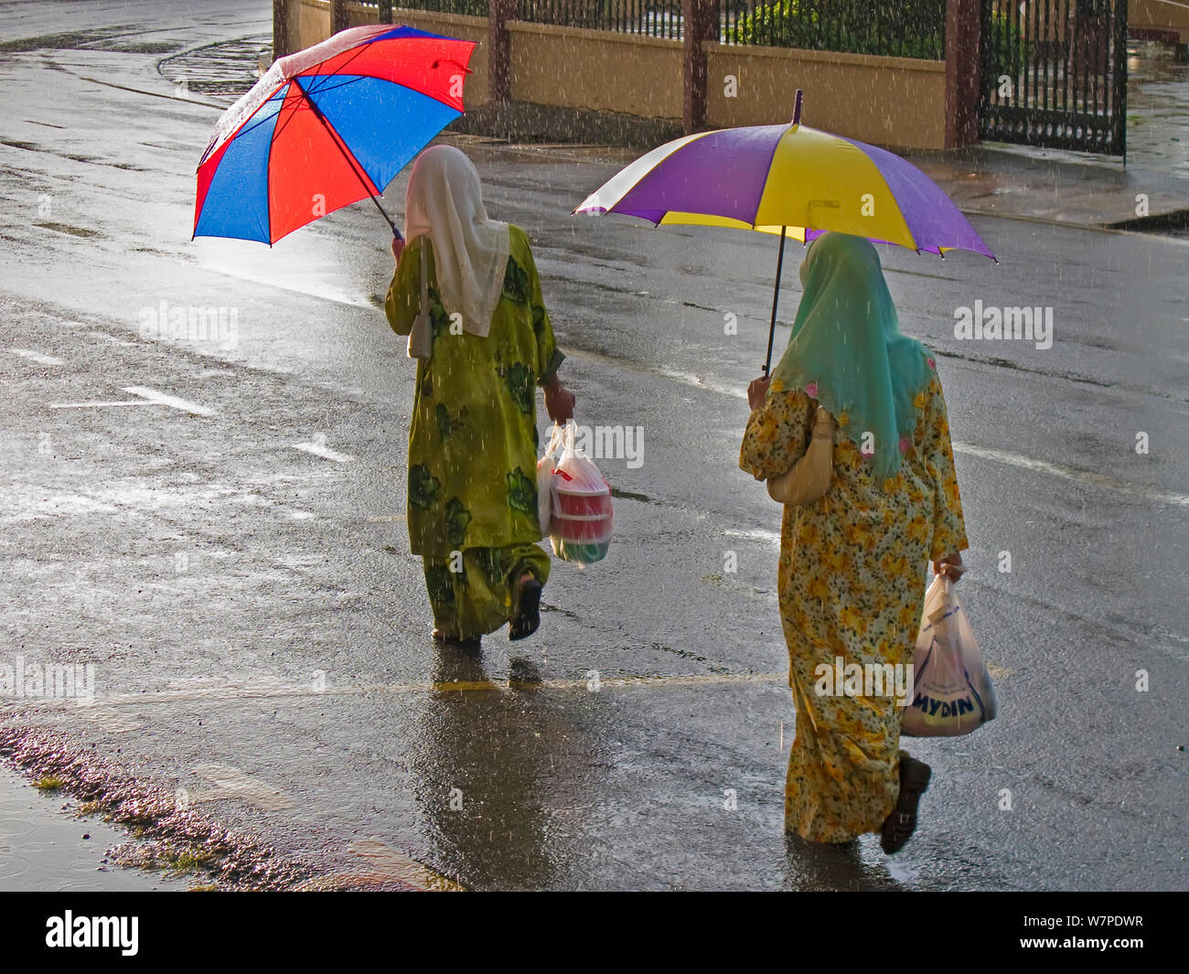 Local muslim woman walking in the rain holding colourful umbrellas ...