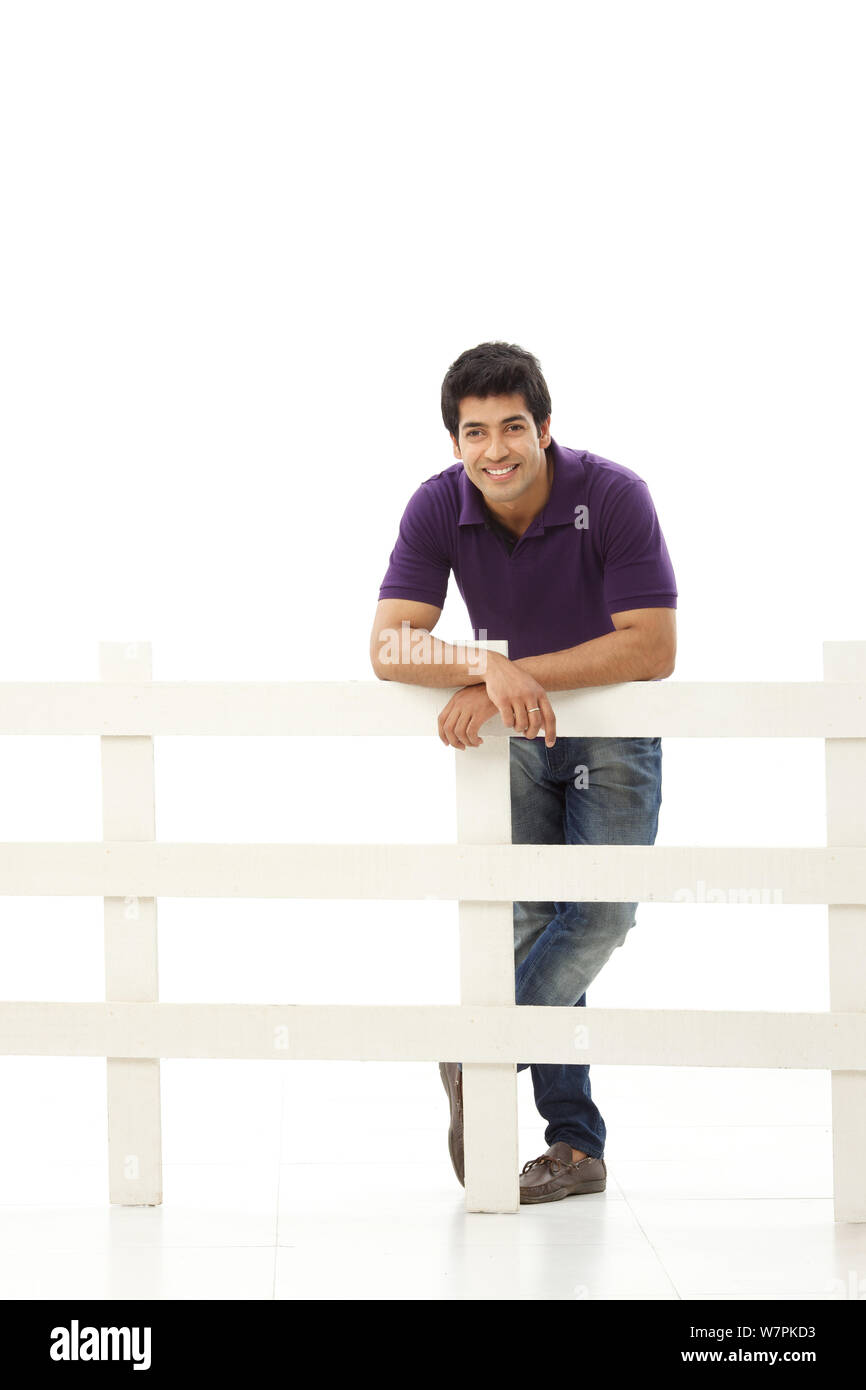 Young man leaning against a railing smiling Stock Photo - Alamy