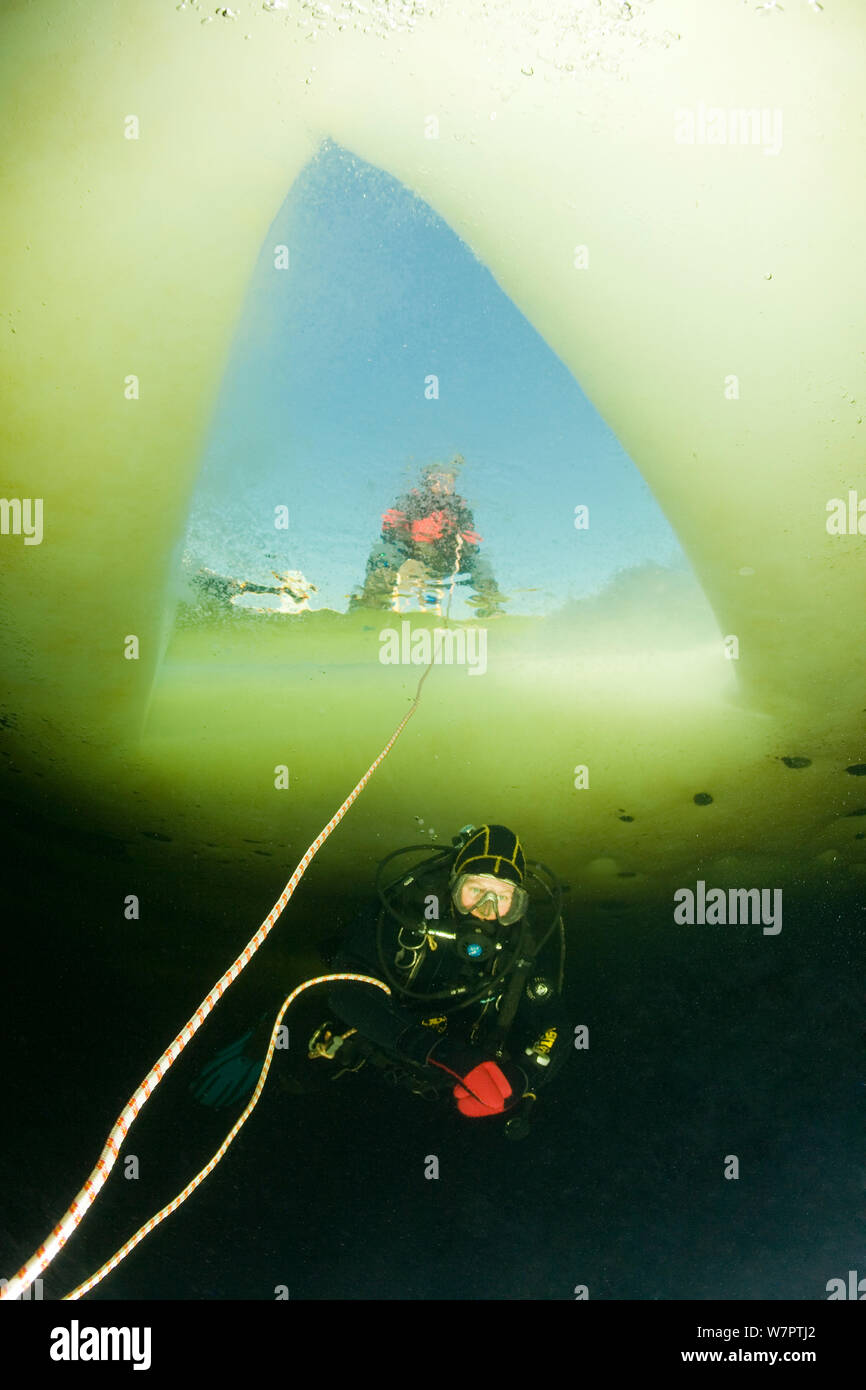 Scuba diver surfacing with person holding rope visible through hole in ...
