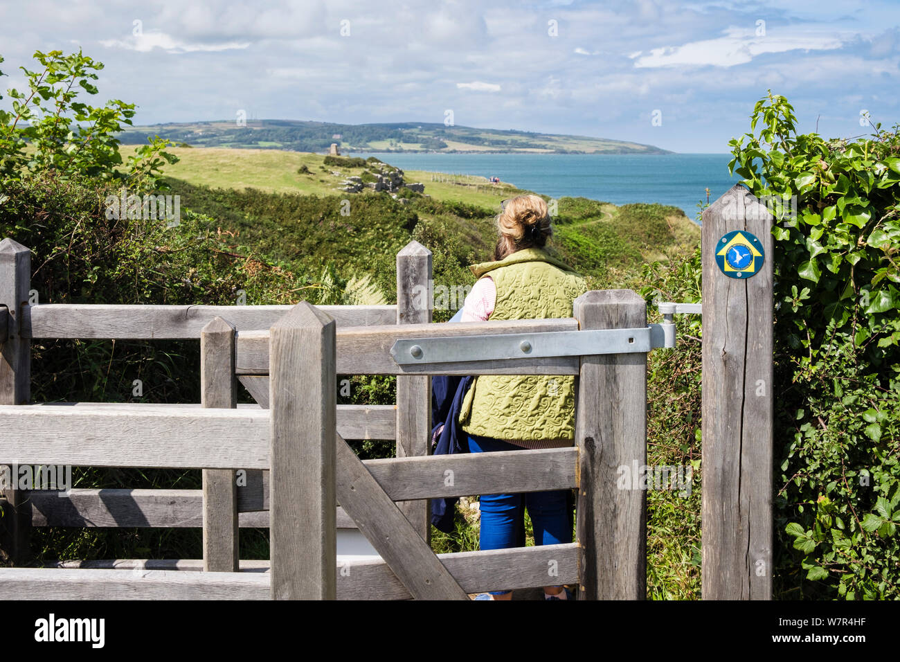 Walker hiking through a kissing gate on Wales coastal path with view to ...