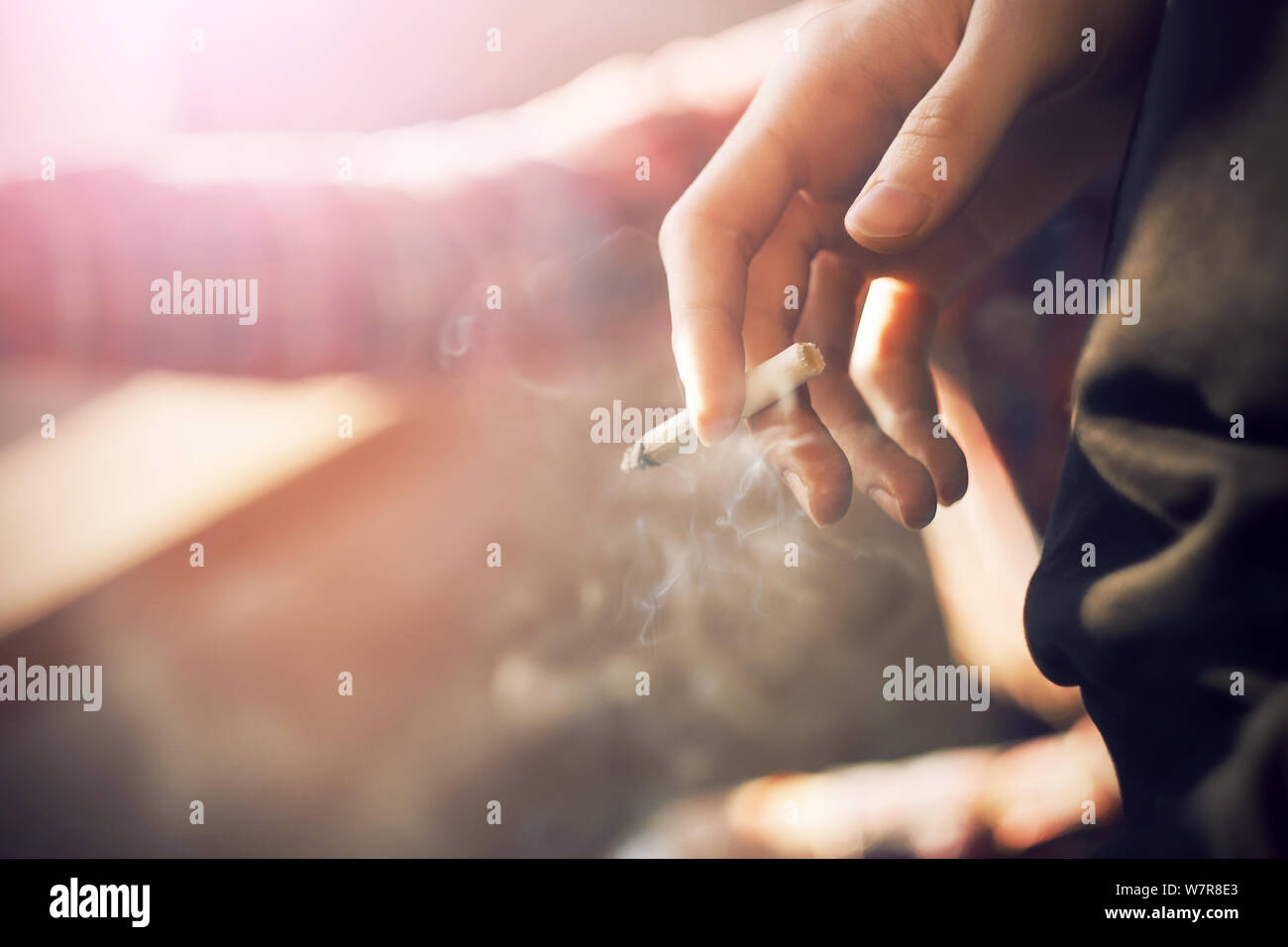 A man's hand with long elegant fingers holds a Smoking cigarette, lit ...