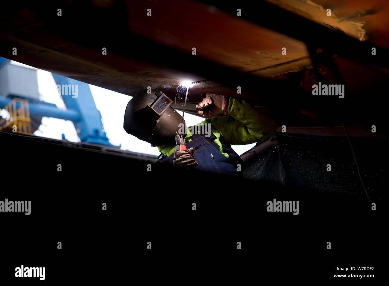 Welder working on underside of hull of large ship Stock Photo - Alamy