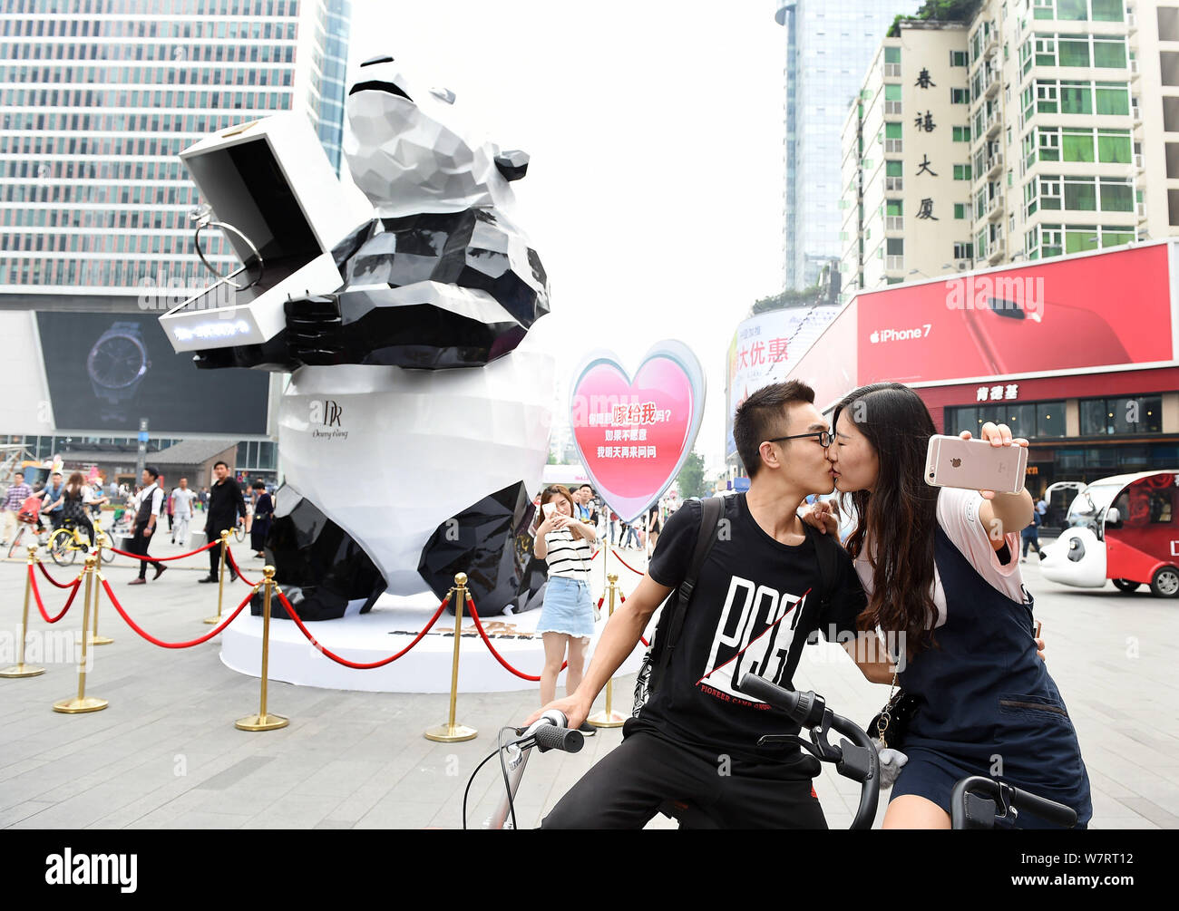 A Chinese couple kisses in front of a giant panda sculpture holding a ...