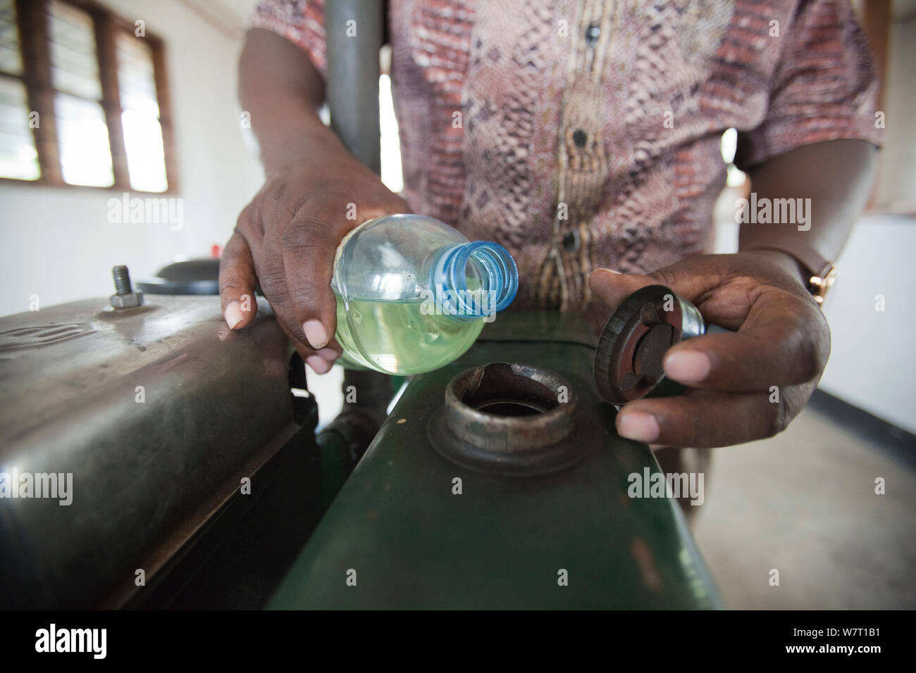 Man pouring Jatropha biofuel from a bottle to fuel a milling machine ...