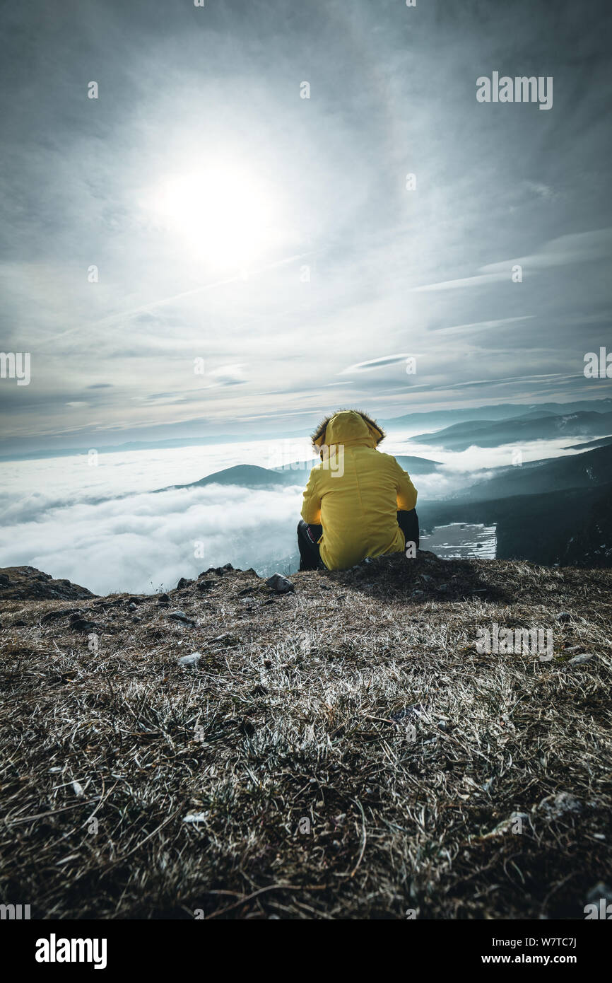 Hiker man take a rest on mountain peak. Man sit on sharp summit and ...