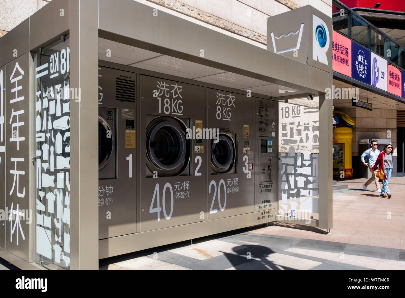 Pedestrians walk past public washing machines installed outside a ...