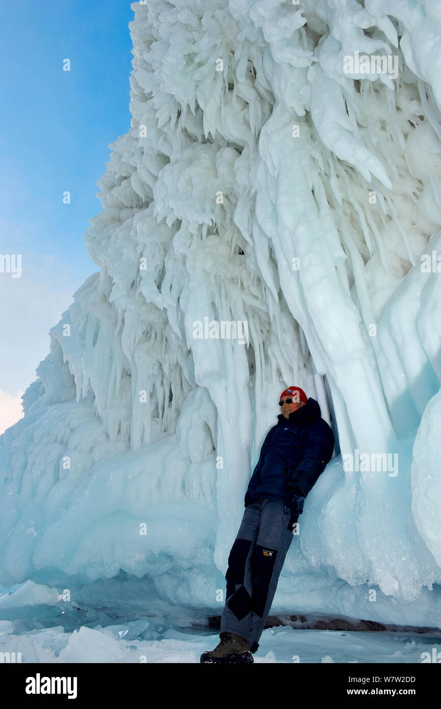 Man standing underneath cliff of large icicles, Lake Baikal, Siberia ...