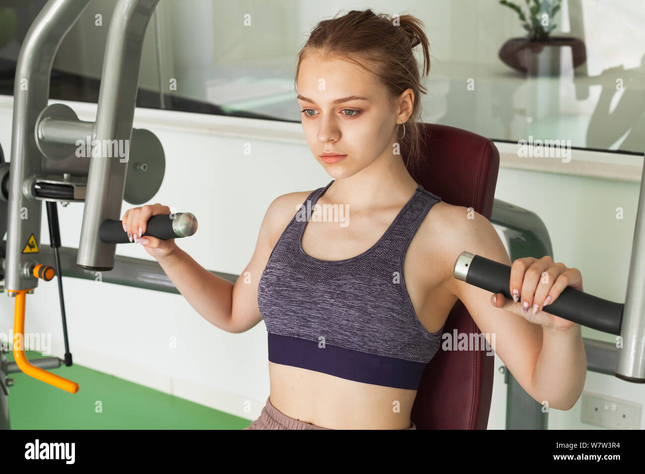 Young Beautiful Blond Sporty Girl Does Machine Chest Press Exercise In