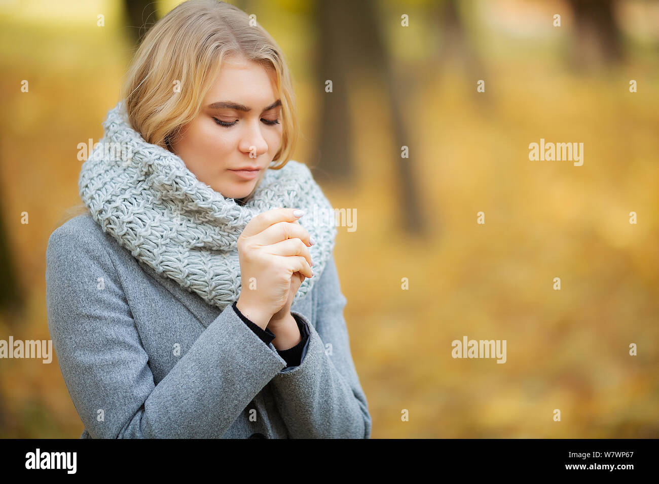 Cold and flu. Young woman in a gray coat walking in the autumn park and ...