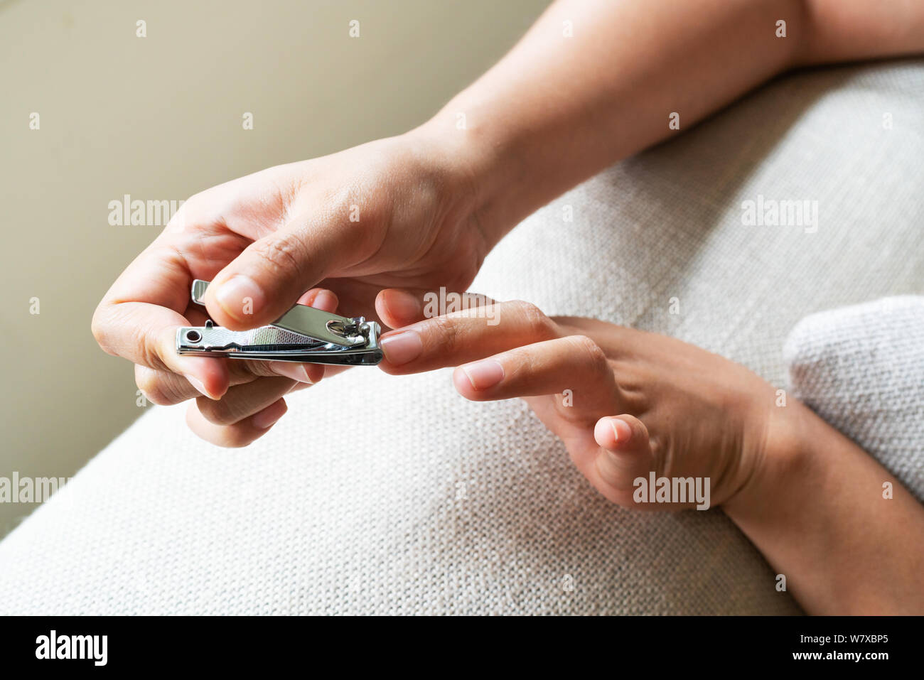 woman hand cutting nails using nail clipper on sofa at living room ...