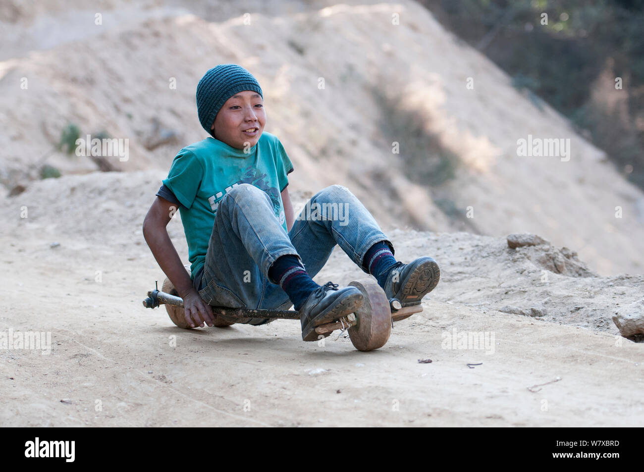 Boy playing with homemade slide toy on wheels. Dirang, Arunachal ...