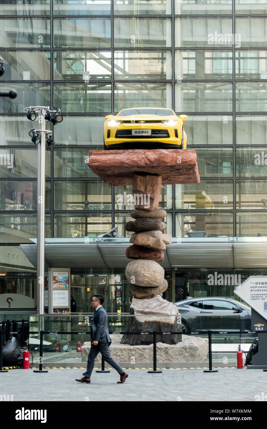 A pedestrian walks past an art installation of a sports car balancing ...