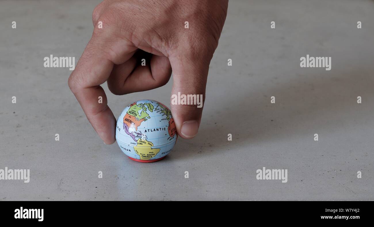 Fingers grabbing a small globe with grey concrete background seen from ...