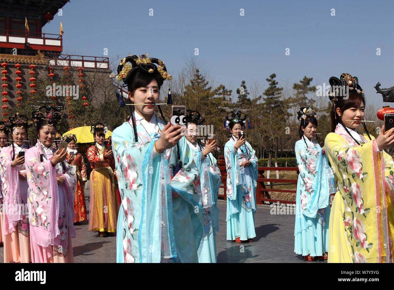 Chinese tour guides dressed in traditional Han costumes bite chopsticks ...