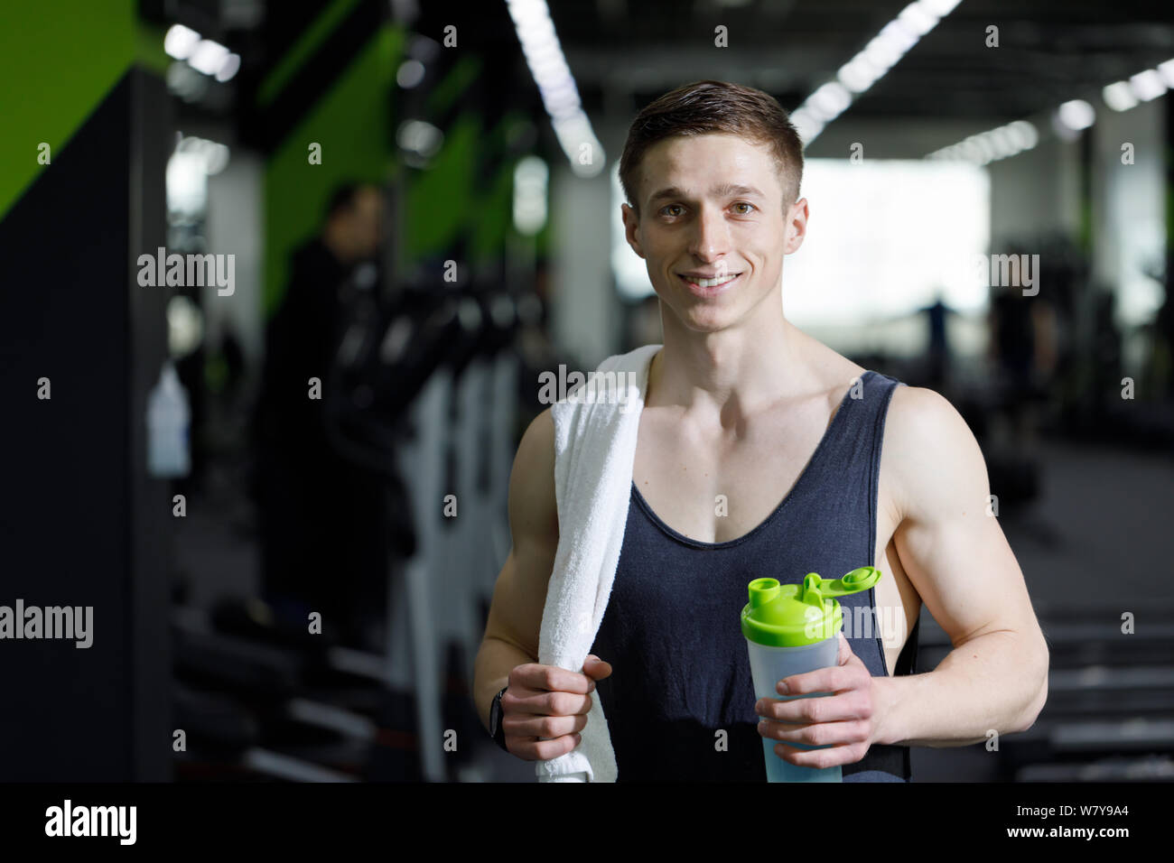 Cheerful young fitness man with towel and bottle of water walking on ...