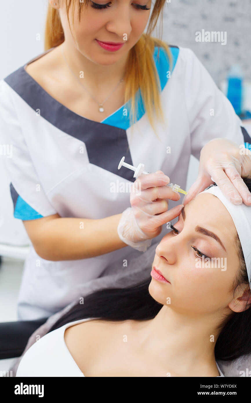 Hands of cosmetologist making injection in face, lips. Young woman gets ...