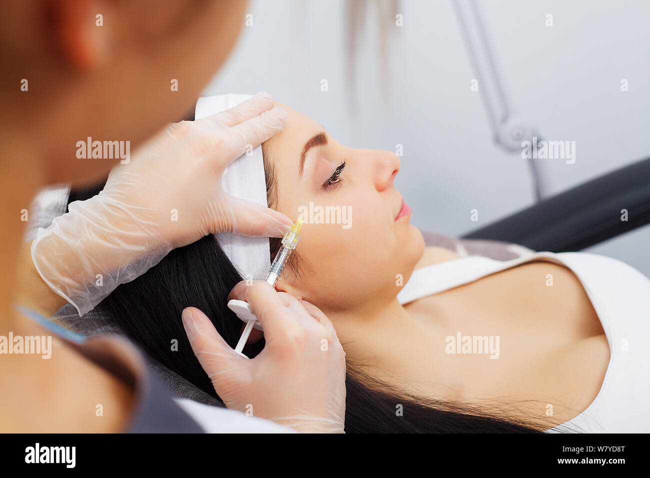 Hands of cosmetologist making injection in face, lips. Young woman gets ...