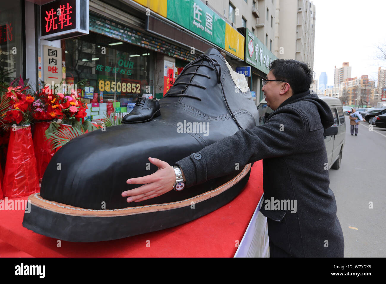 A pedestrian measures the giant shoe with his hands on display in ...