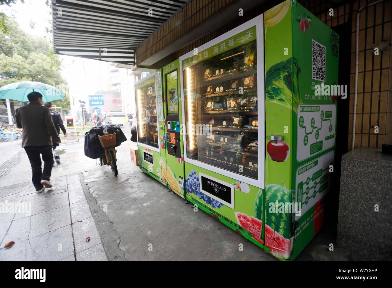 Pedestrians walk past vegetable vending machines on a street in ...