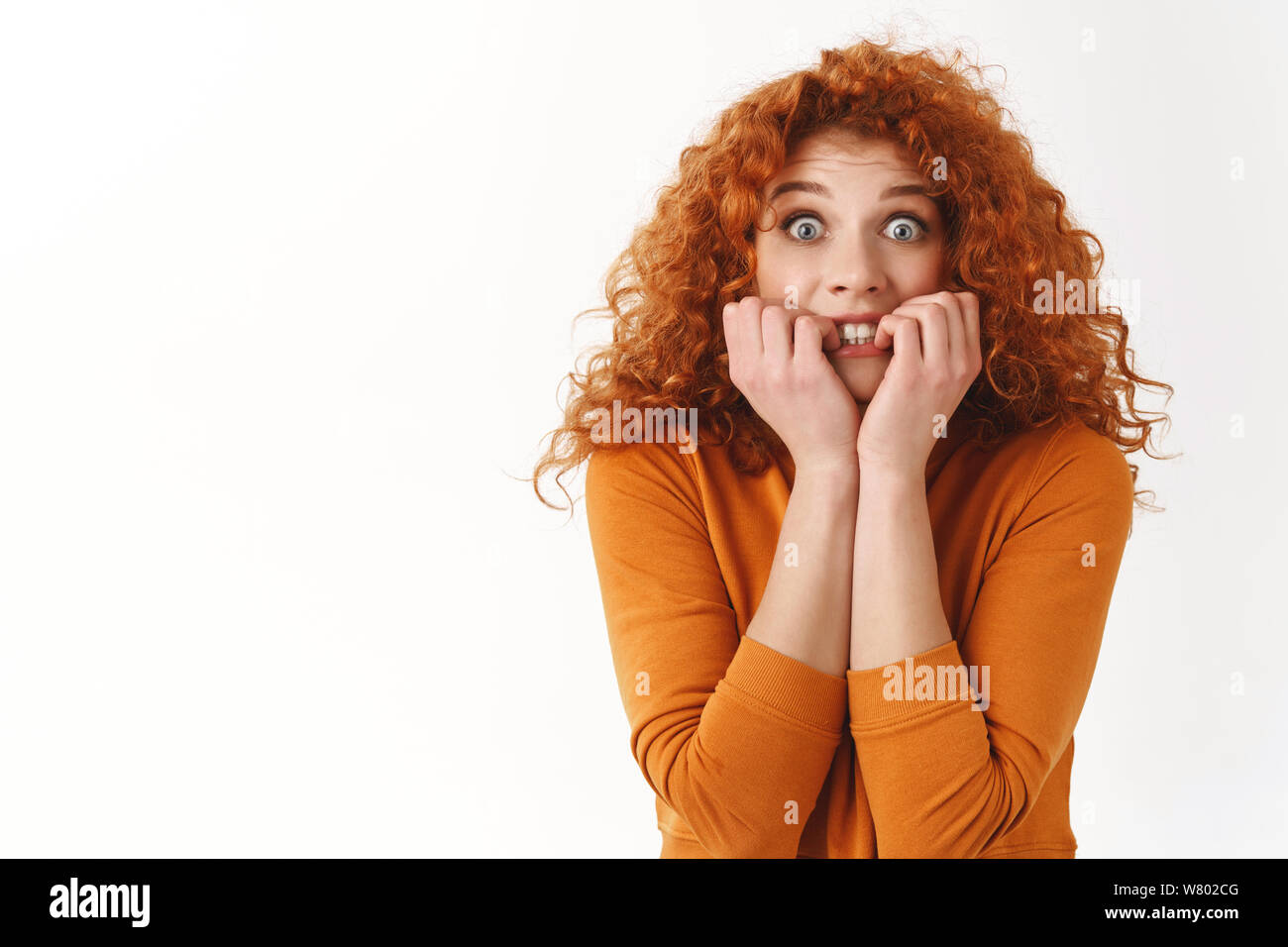 Scared young redhead curly-haired woman biting fingers, trembling fear ...