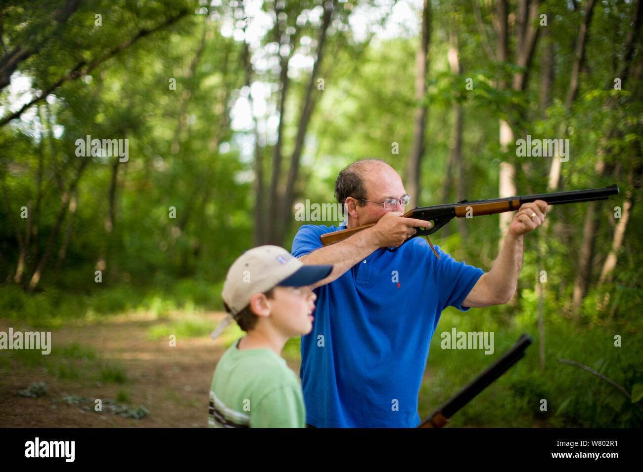 Man and young boy aiming rifles in forest Stock Photo - Alamy