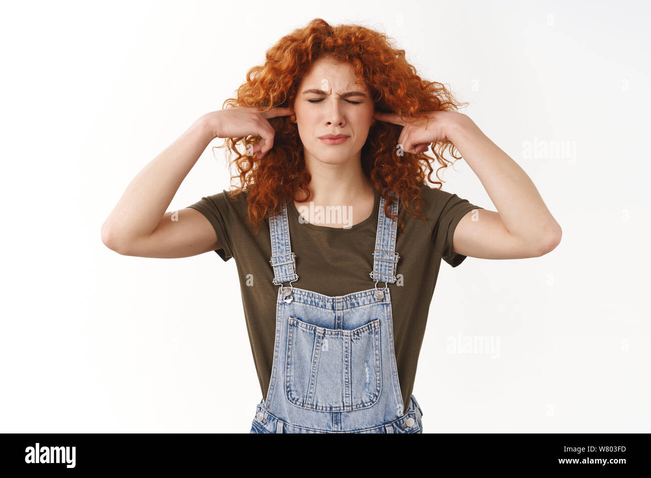 Annoyed and pissed curly-haired ginger girl plug fingers into ear holes ...