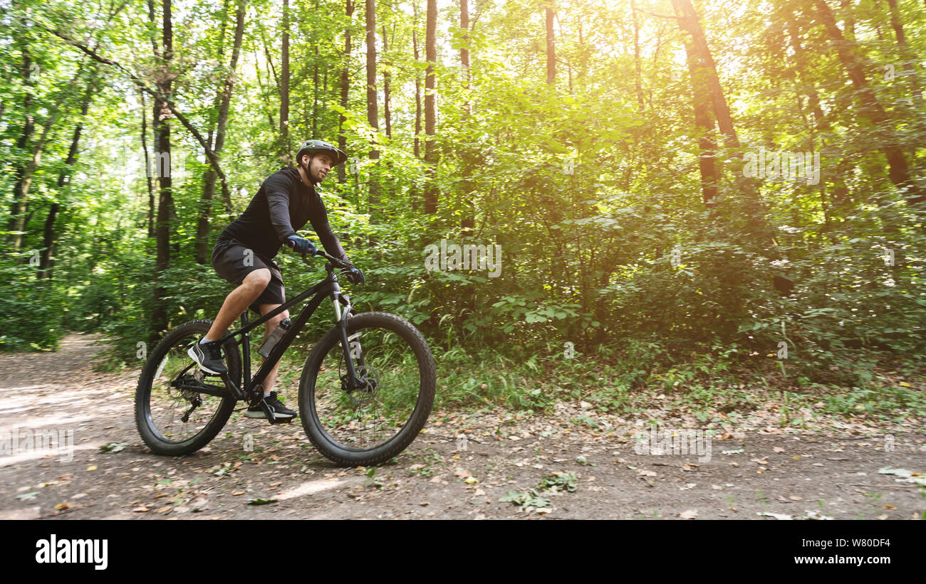 Male sportsman riding bike along forest road Stock Photo - Alamy