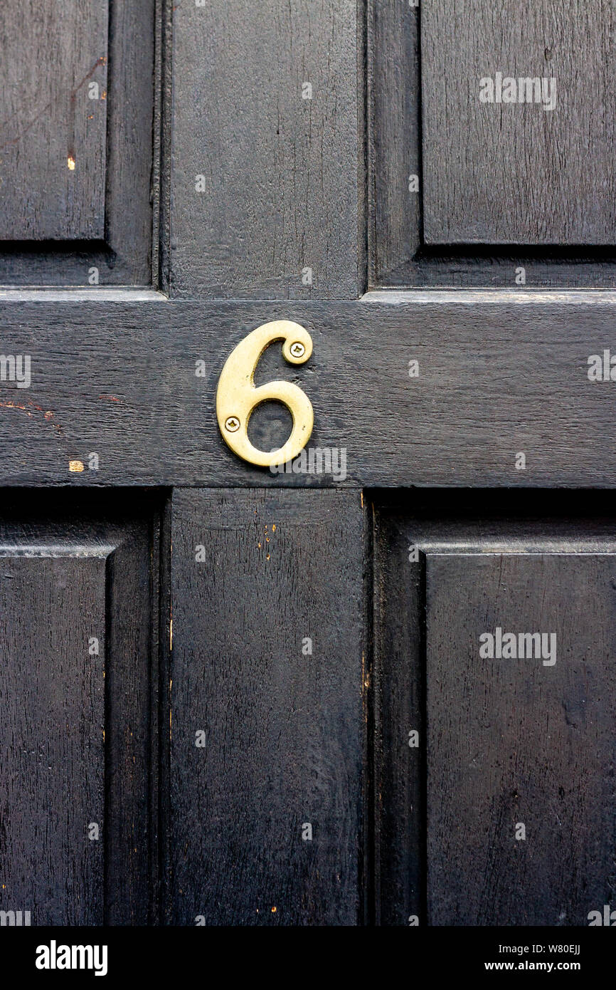 Bronze house number 6 with the six centred on an old black wooden front ...